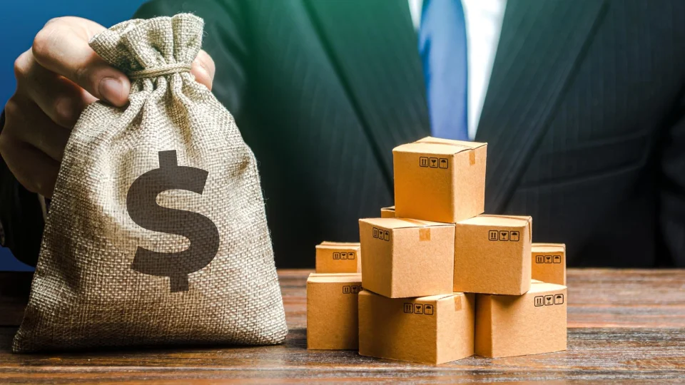 A person in a suit holds a burlap money bag next to stacked mini ...