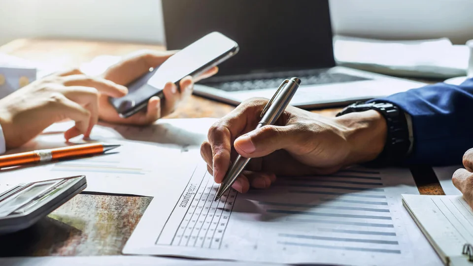 Two people sit at a desk reviewing an expense document together with a ...